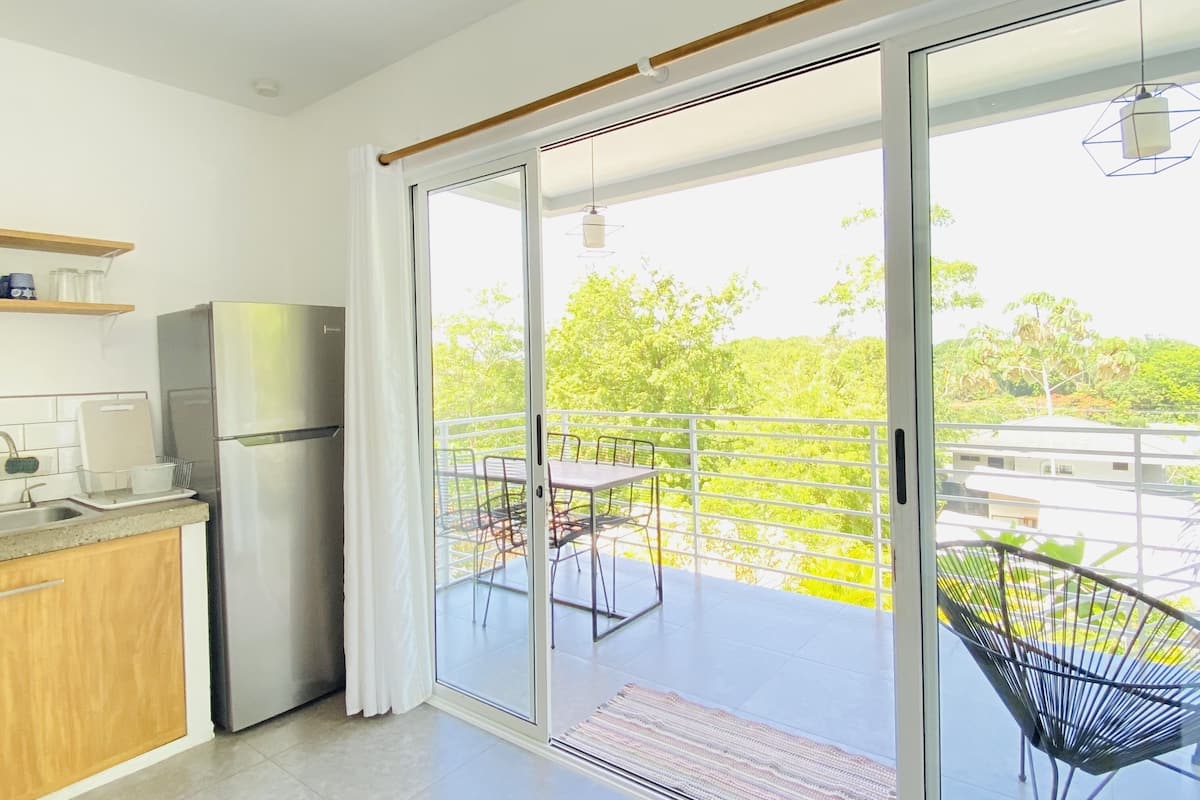 Uma cozinha moderna com geladeira, pia e janela com vista para uma varanda com mesa e cadeiras.