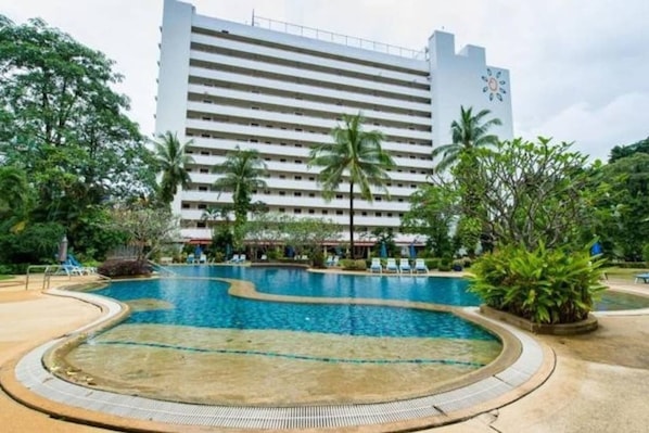 Um hotel com uma piscina grande, palmeiras e um edifício alto ao fundo.