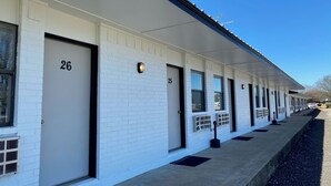 Uma fileira de quartos de motel com paredes de tijolo branco, portas numeradas e janelas pequenas.