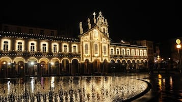 Um edifício histórico com janelas em arco e uma torre central, rodeado por uma fonte refletora.
