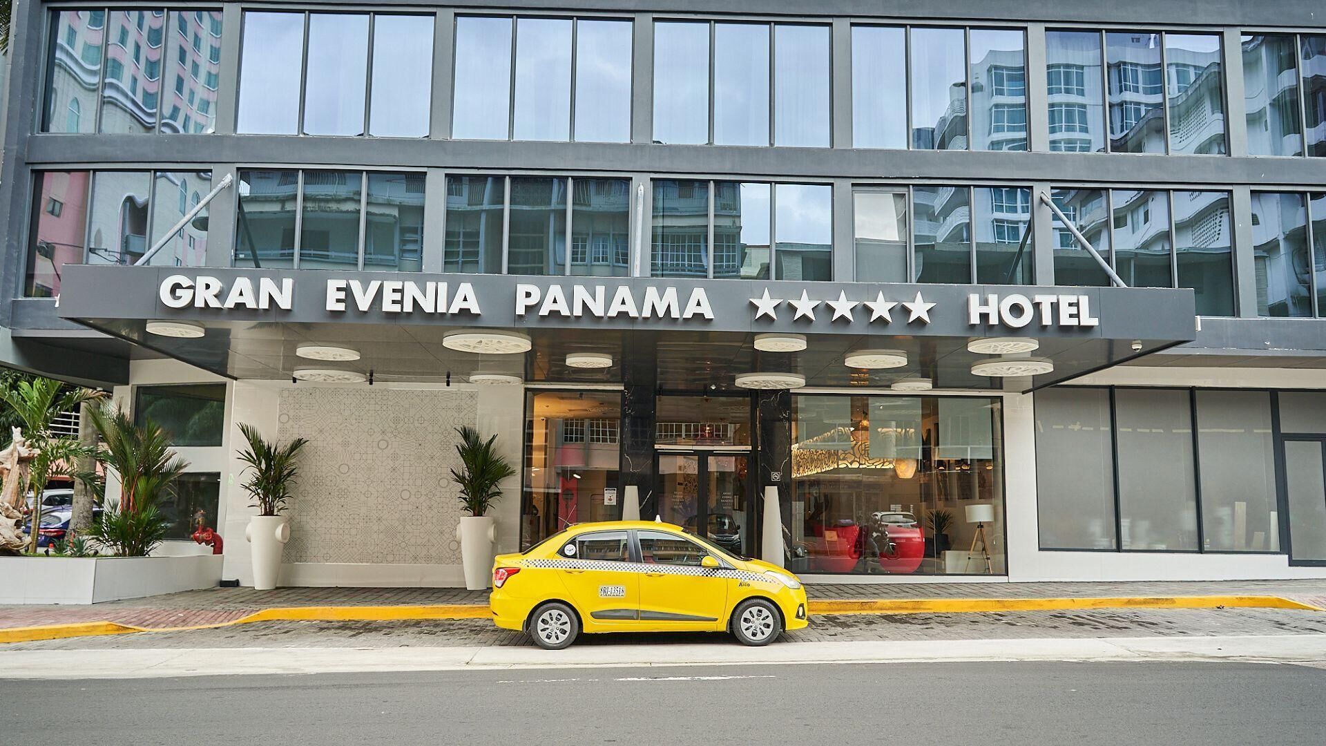 Exterior do Hotel Gran Evnia Panama, com um táxi amarelo estacionado em frente.