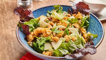 Uma salada em uma tigela, com folhas verdes variadas e croutons, sobre um prato azul.