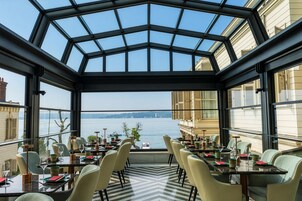 Um restaurante com teto de vidro, mesas postas para refeições e vista para o mar.