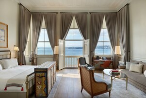 Quarto de hotel com cama, escrivaninha, poltrona e vista para o mar.