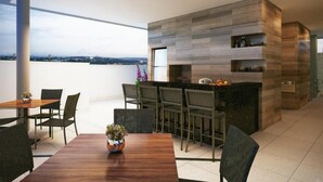 Cozinha moderna com revestimento de madeira e espaço para balcão. Há uma área de jantar com mesa e cadeiras, e vista para a cidade ao fundo.