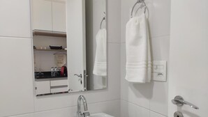Uma casa de banho com uma pia branca, um espelho e duas toalhas penduradas em ganchos.