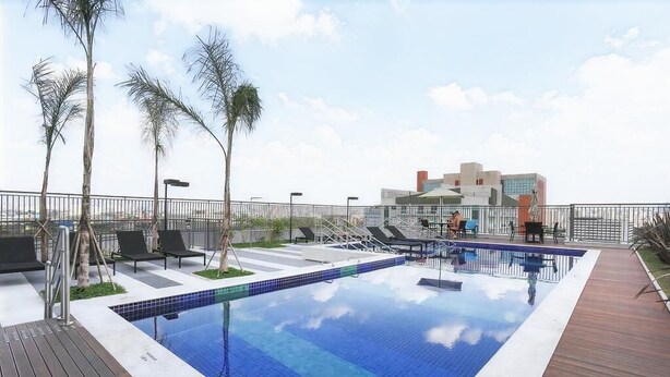Uma área de piscina no terraço com espreguiçadeiras, um deck de madeira e um edifício moderno ao fundo.