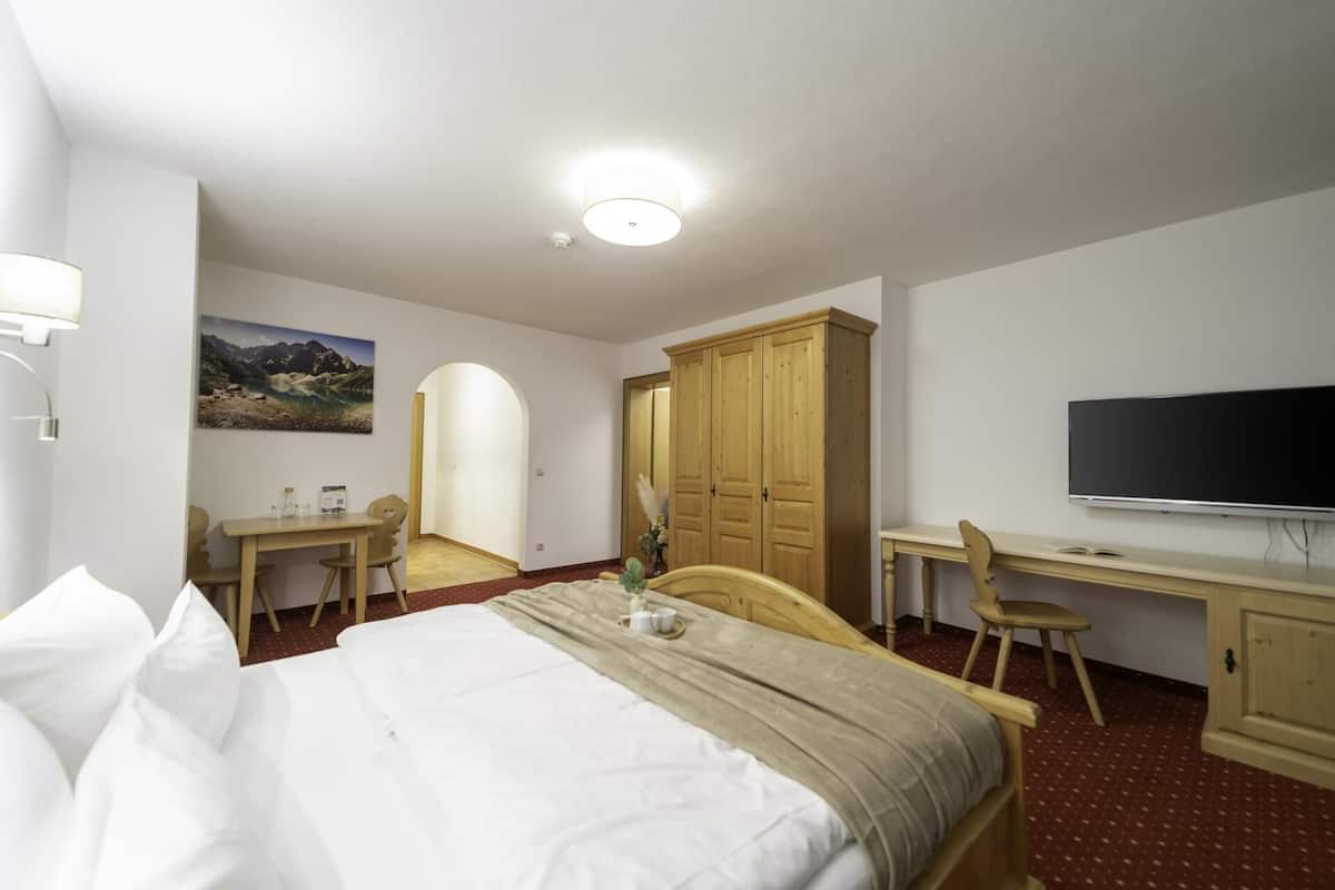 Quarto de hotel com cama, escrivaninha, cadeira, televisão, guarda-roupa e um quadro na parede.