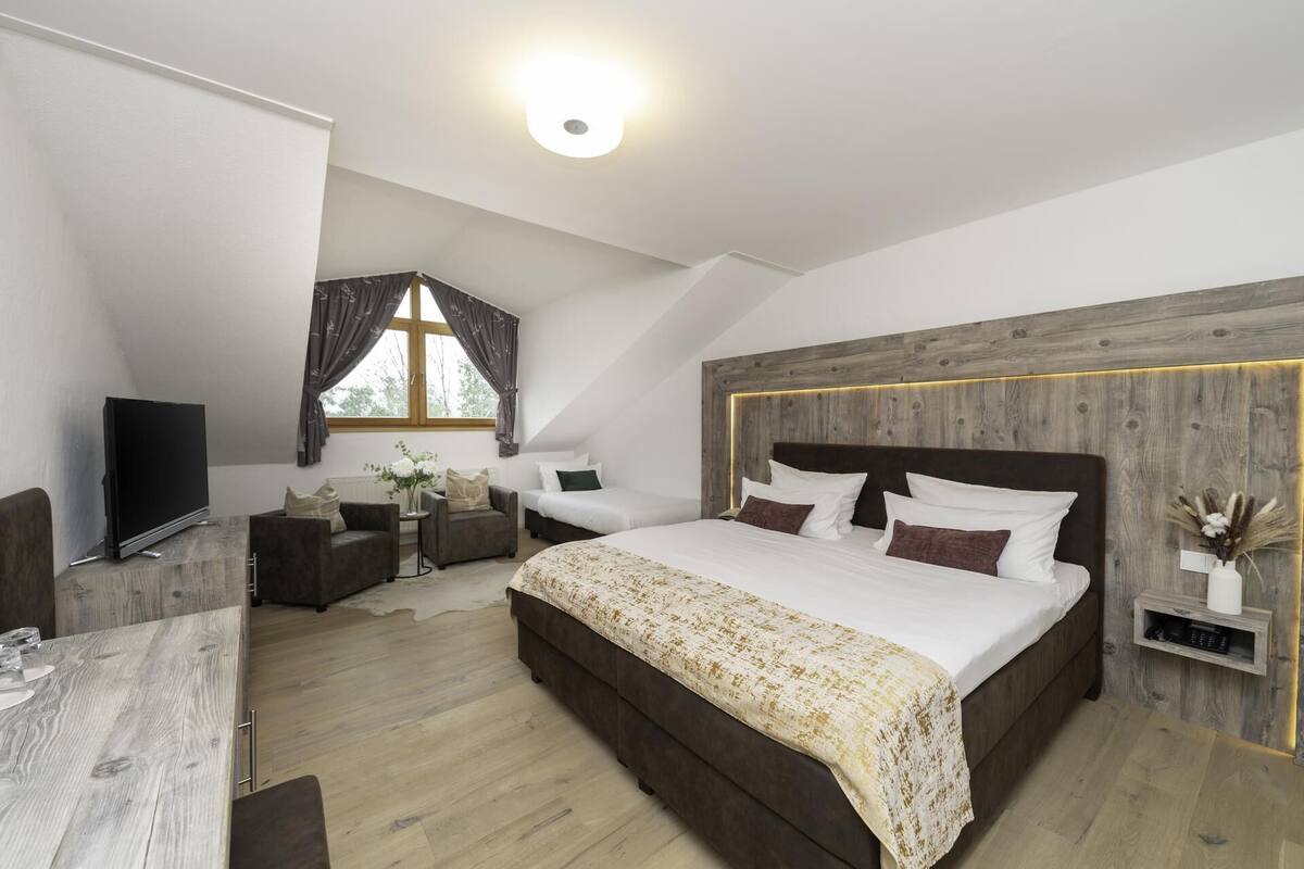 Quarto moderno com uma cama grande, televisão, escrivaninha e janela com cortinas.
