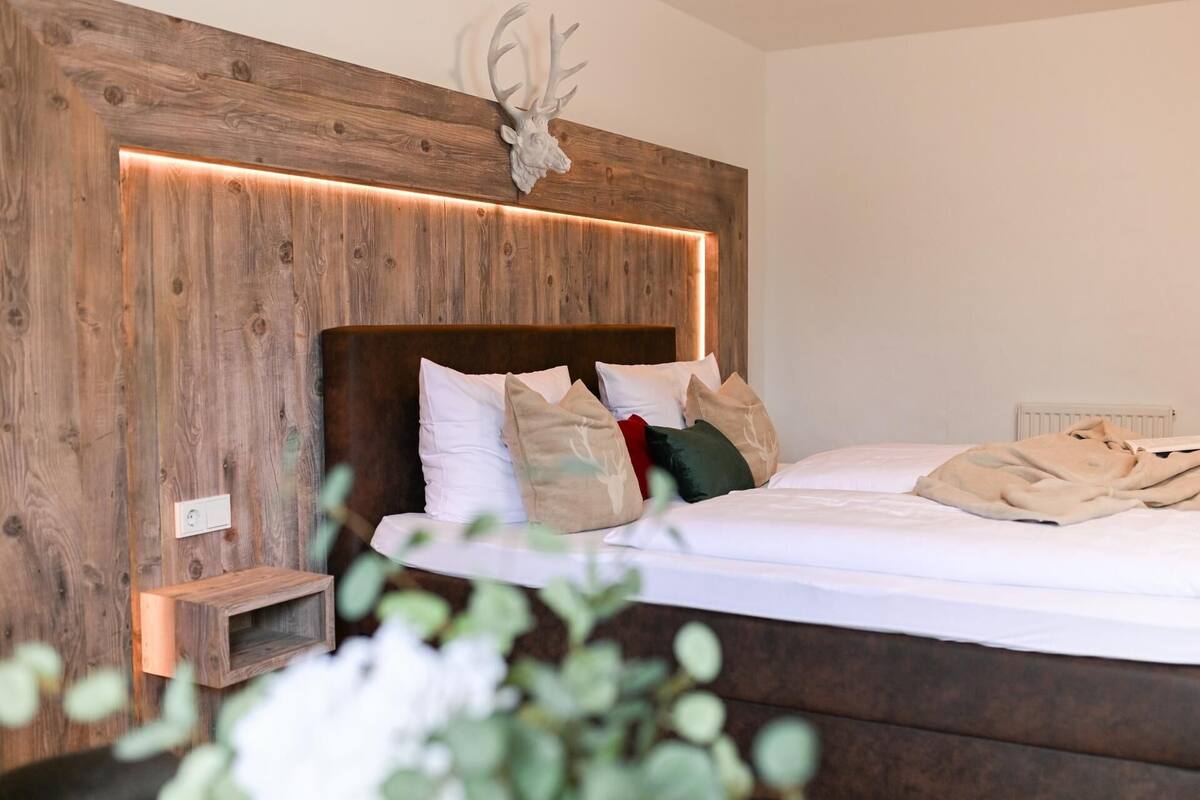Quarto com cabeceira de madeira, cabeça de veado na parede e mesa de cabeceira.