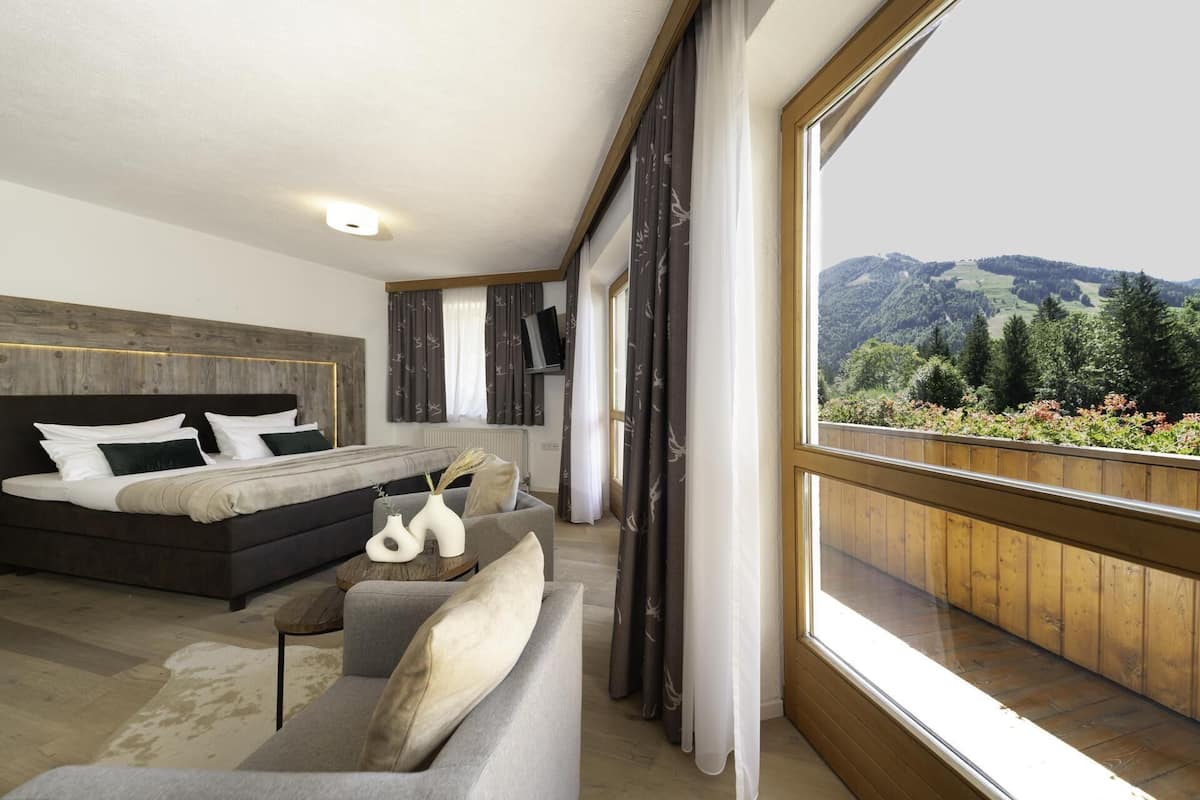 Quarto com uma cama grande, um sofá e vista para uma paisagem montanhosa através de uma varanda.