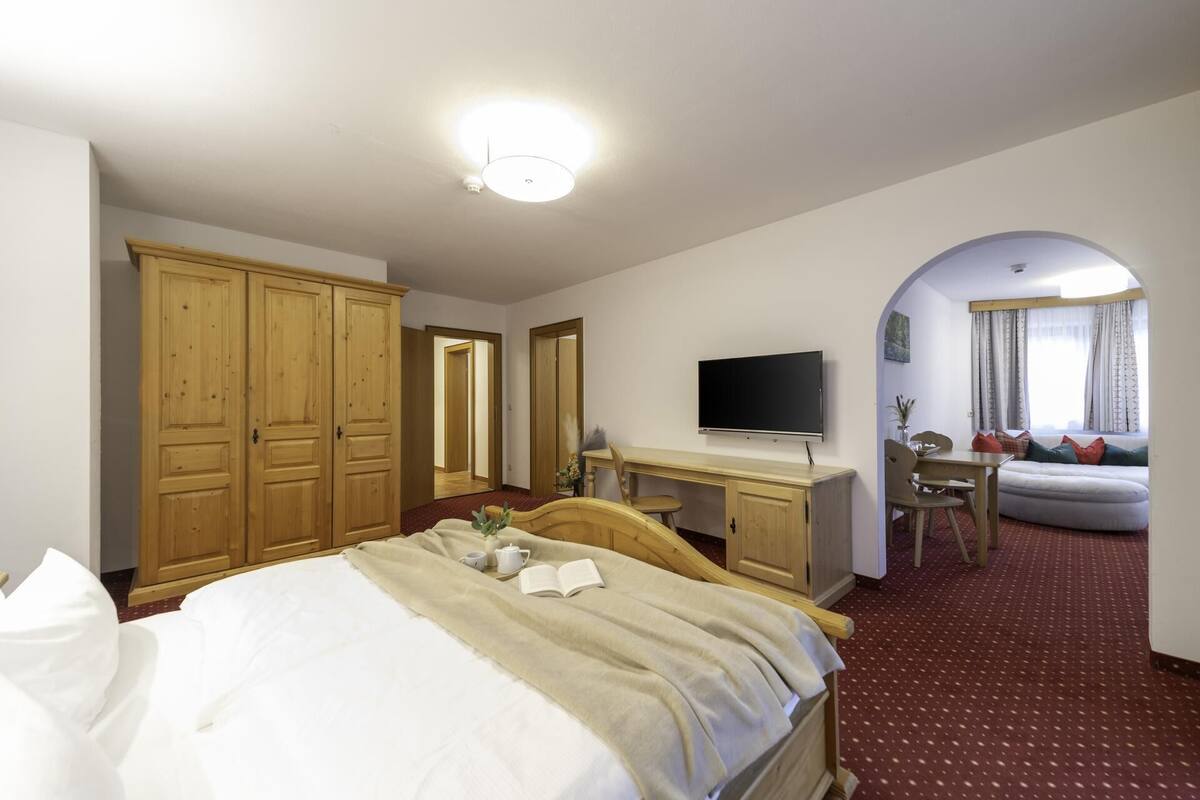Quarto de hotel com uma cama, uma escrivaninha com cadeira, uma televisão e um sofá.