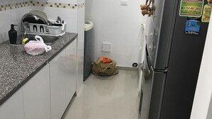 Uma cozinha pequena com armários brancos, bancada de granito, geladeira preta e painel de azulejos.