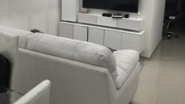 Uma sala de estar moderna com um sofá branco, uma televisão de tela plana fixada em um móvel branco e um candelabro.