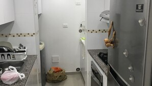 Uma cozinha compacta com armários brancos, uma geladeira de aço inoxidável e uma pia.