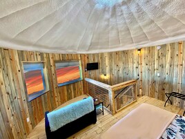 Quarto com paredes de madeira, um sofá, uma cama, uma lareira e duas pinturas.
