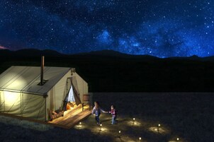 Acomodação em tenda com vista para um céu estrelado, lareira interna e uma criança brincando ao ar livre.