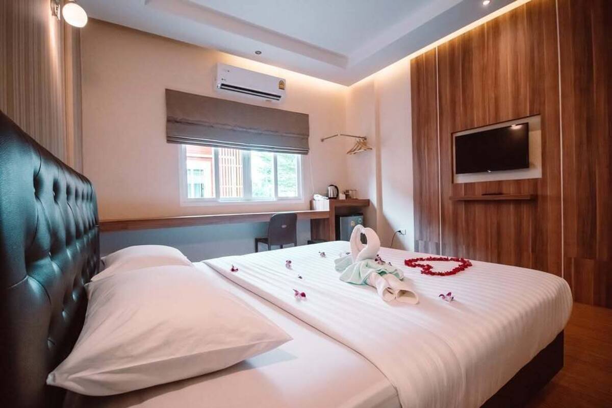 Quarto de hotel com uma cama grande, televisão de tela plana na parede, escrivaninha com cadeira e uma janela com persianas.