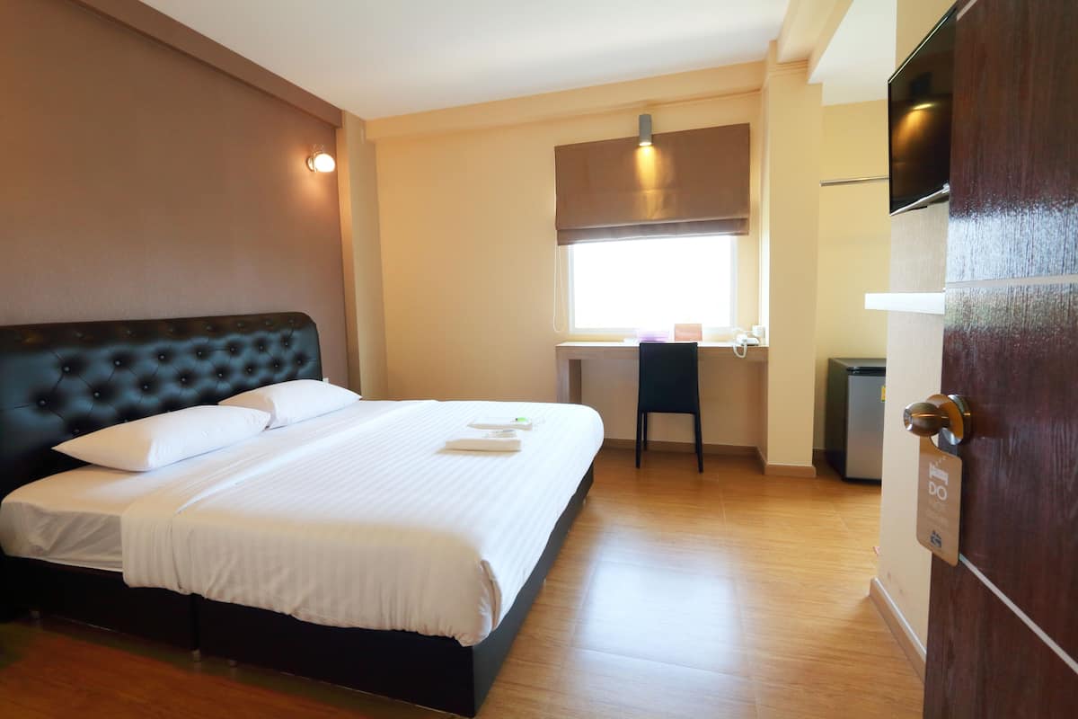Quarto de hotel com uma cama grande, uma escrivaninha e uma televisão.