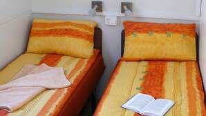 Duas camas de solteiro com roupa de cama listrada em laranja e amarelo, uma pequena prateleira acima e um livro em uma das camas.