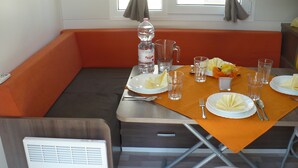 Uma área de refeições com uma mesa posta para dois, incluindo pratos, talheres, copos e uma garrafa de água.