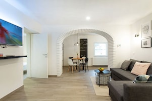 Uma sala de estar moderna com um sofá, uma televisão, um espaço de jantar com cadeiras e uma bancada de cozinha.