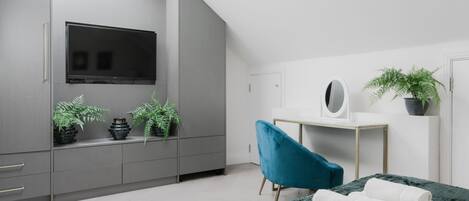 Um quarto moderno com um guarda-roupa cinzento, uma televisão de ecrã plano, uma cadeira azul, uma cama com toalhas brancas dobradas e uma planta num vaso.