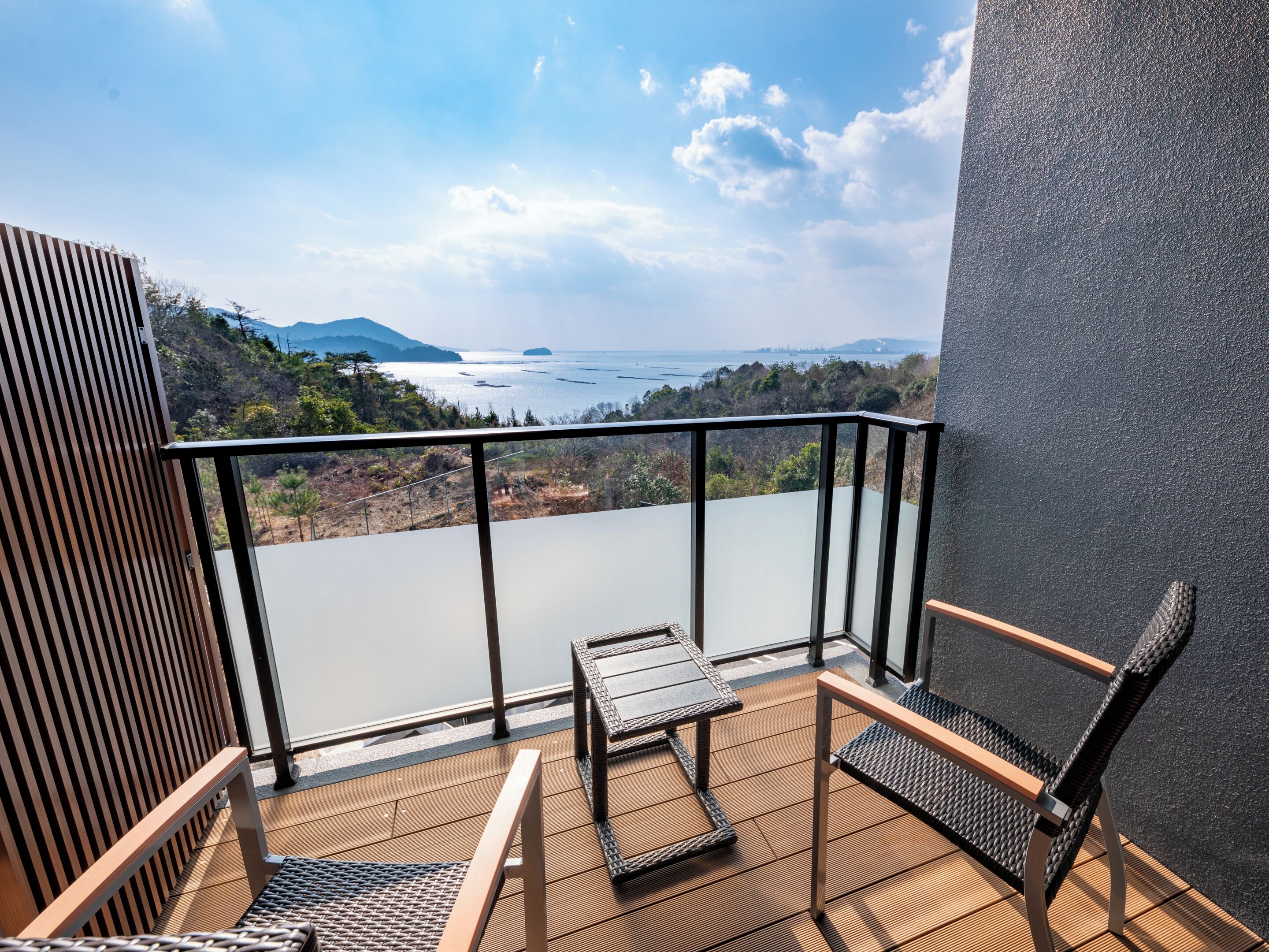 Uma varanda com vista para a água, uma cadeira e uma mesa pequena.