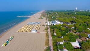 Vista aérea de uma praia com fileiras de guarda-sóis e cadeiras de praia, um farol e uma combinação de edifícios residenciais e comerciais.