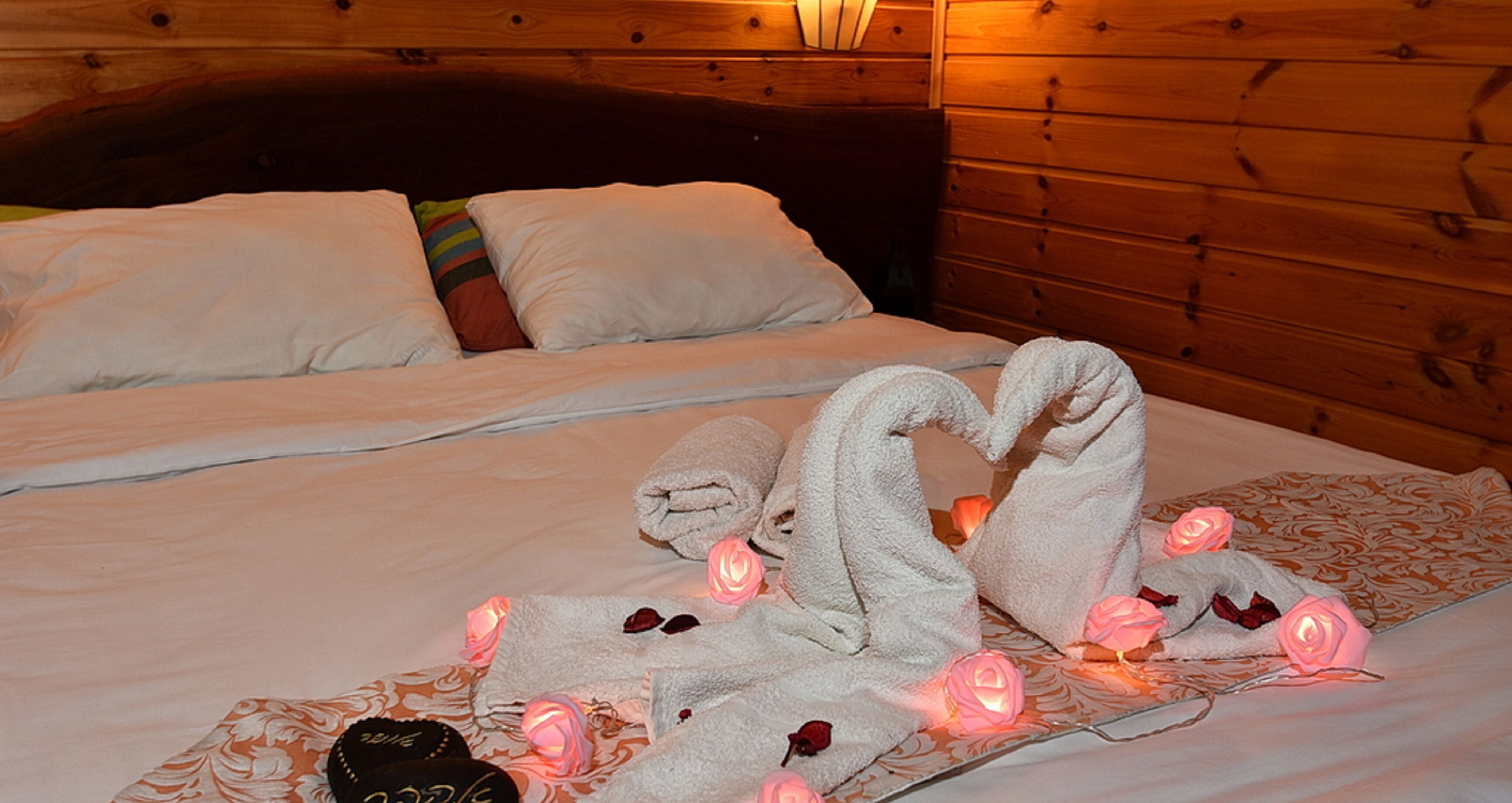 Uma cama bem arrumada com lençóis brancos, arranjo de toalhas em formato de coração e decorações de rosas cor-de-rosa.