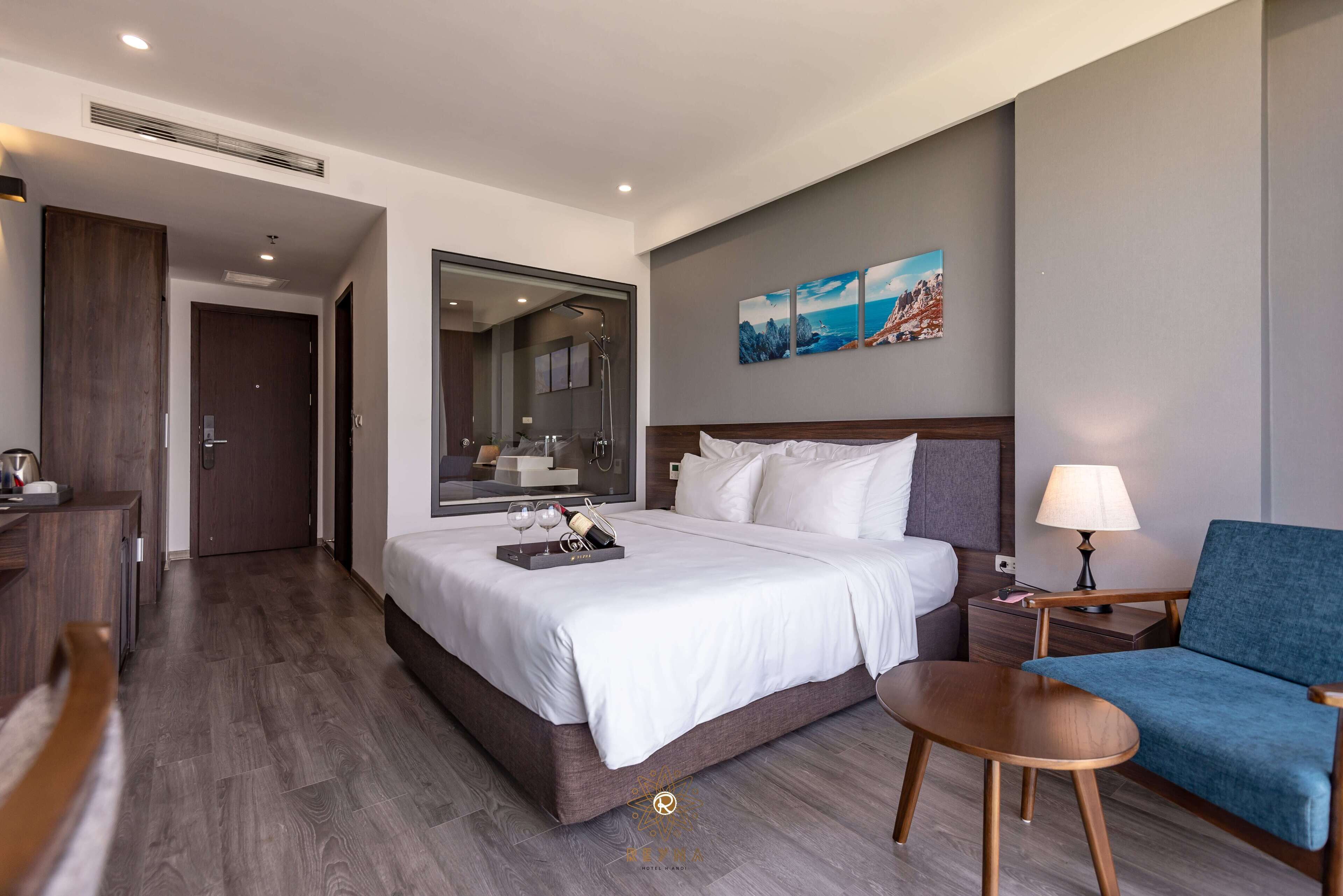 Quarto de hotel com uma cama grande, uma escrivaninha, uma cadeira, uma mesa pequena e um quadro na parede.