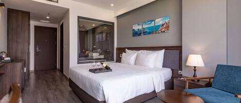 Quarto de hotel com uma cama grande, uma escrivaninha, uma cadeira, uma mesa pequena e um quadro na parede.