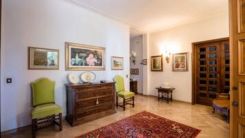 Um corredor com piso de madeira, cadeiras verdes, um tapete estampado em vermelho e quadros nas paredes.