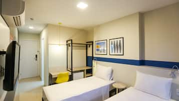Quarto de hotel com duas camas, uma escrivaninha, uma cadeira e uma mesinha.