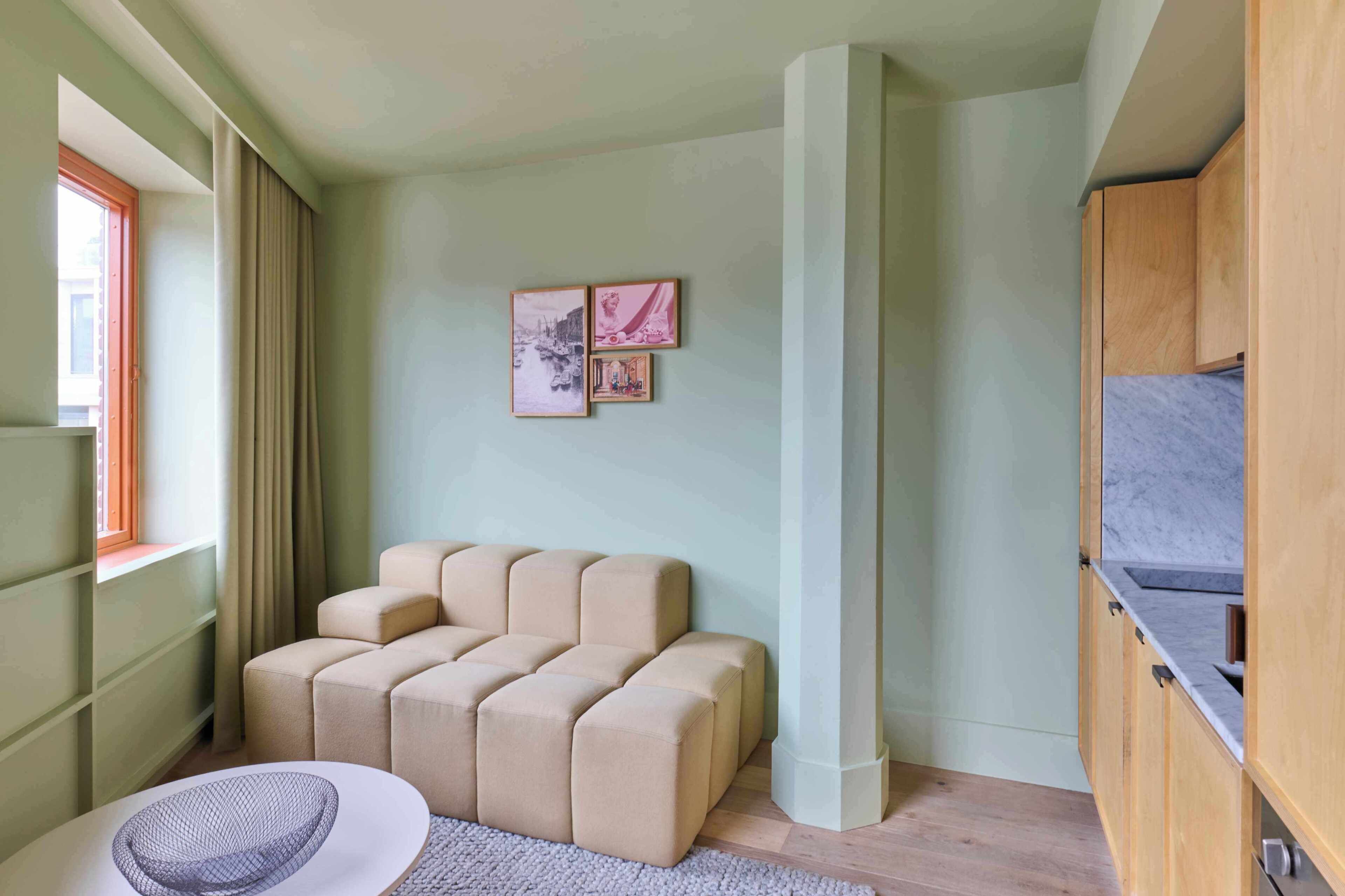 Um quarto com um sofá bege, uma mesinha redonda e um armário de madeira.