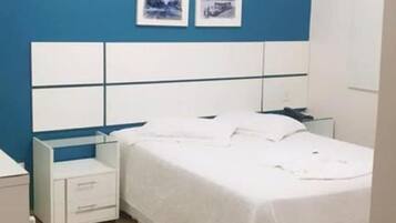 Quarto com cama, mesas de cabeceira, cômoda e duas imagens emolduradas na parede.