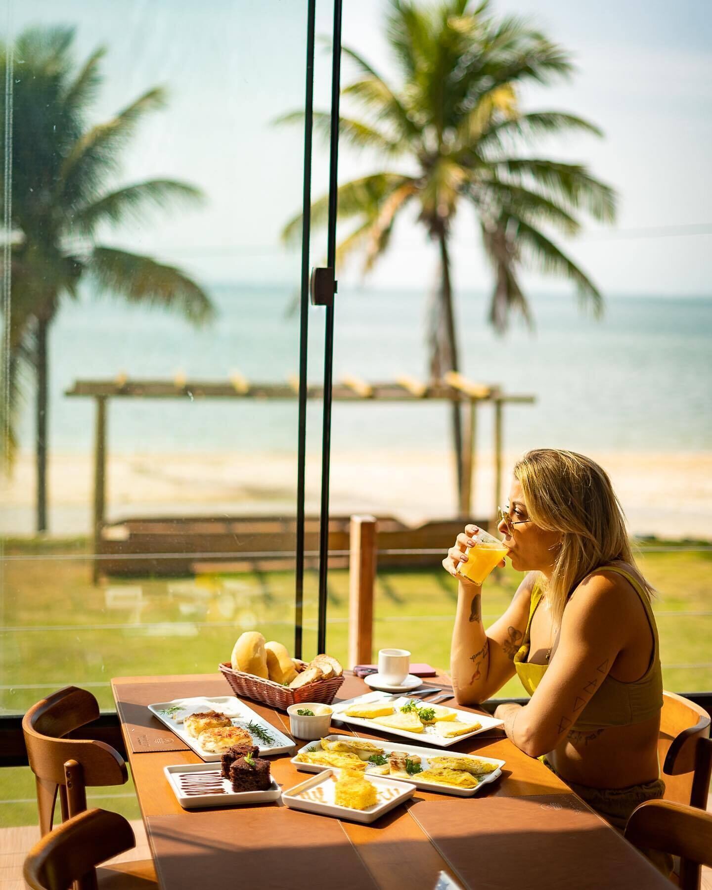 Uma mesa de jantar com diversos pratos, uma janela com vista para uma praia e palmeiras, e vista para o oceano.