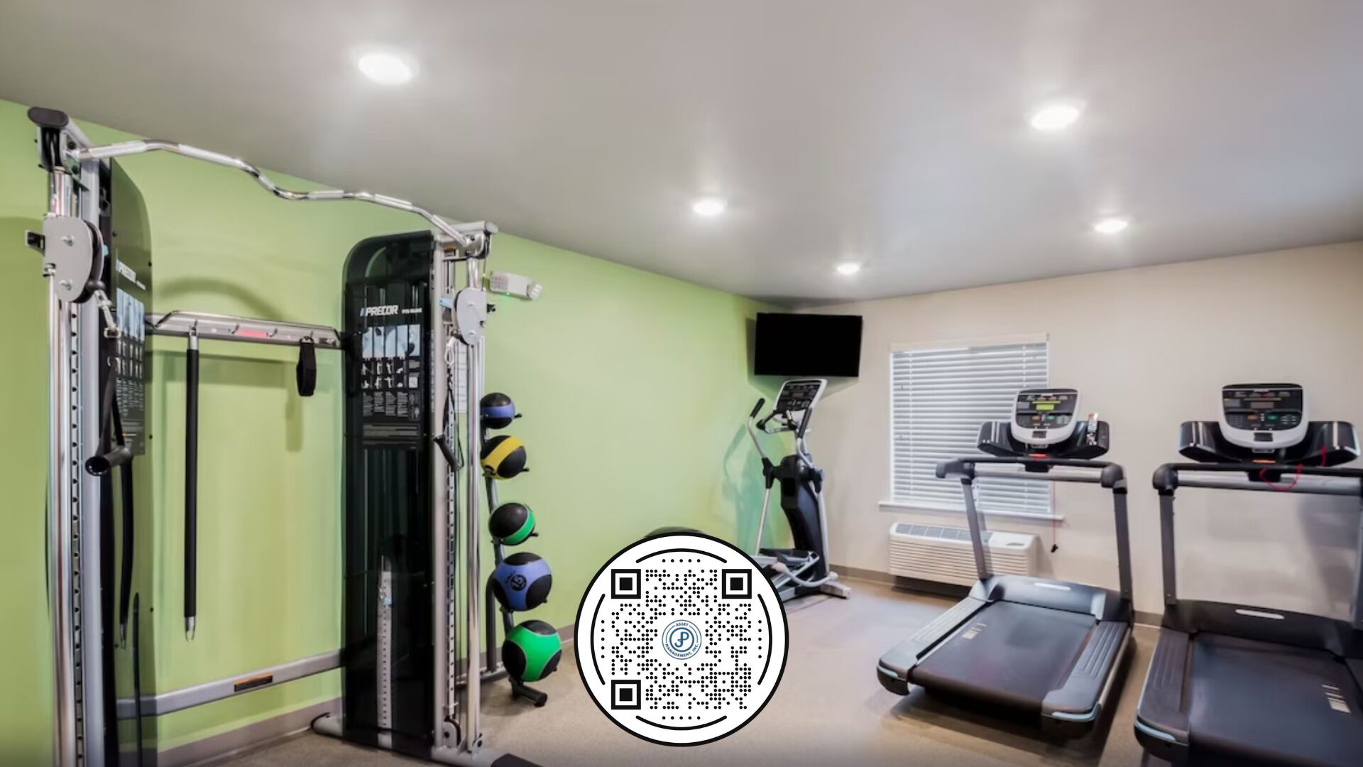 Uma academia com equipamentos de exercícios, esteiras e uma TV fixada na parede.