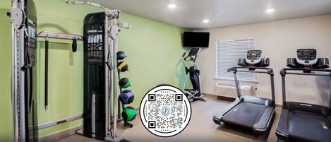 Uma academia com equipamentos de exercícios, esteiras e uma TV fixada na parede.