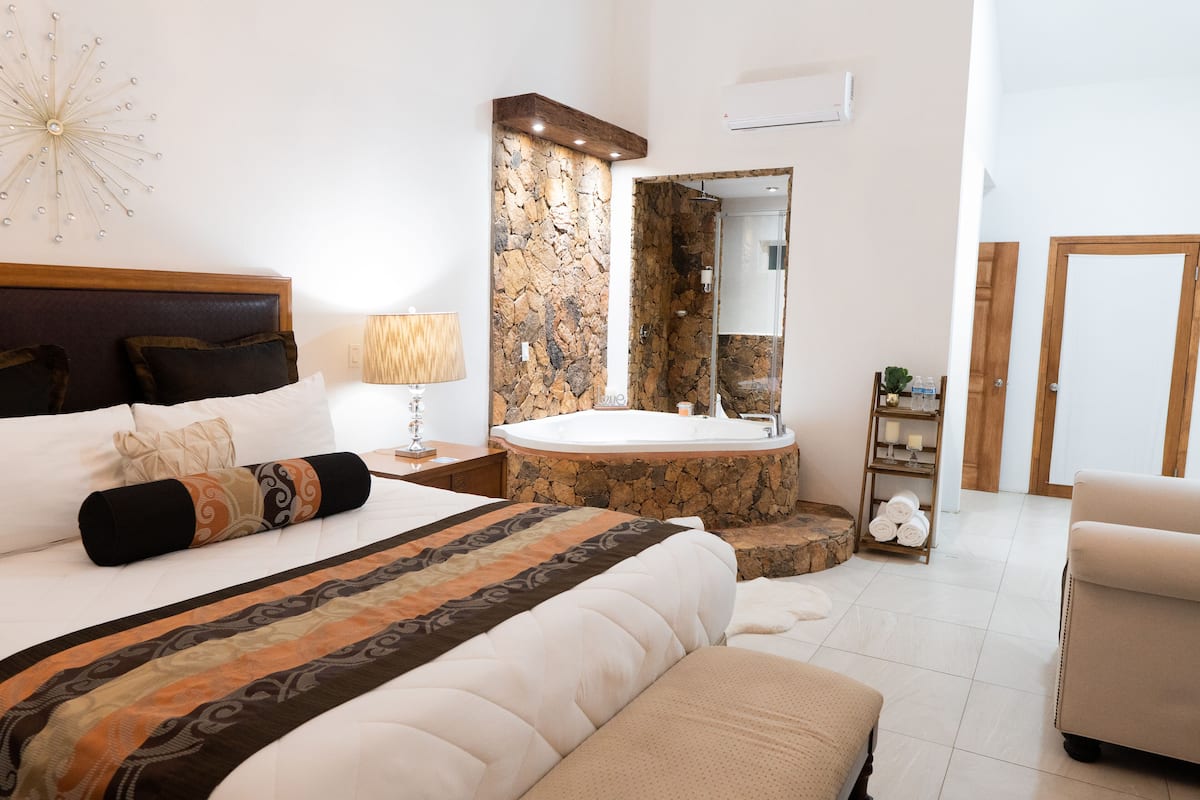 Quarto de hotel com uma cama grande, parede de pedra, banheira e um espaço para sentar.