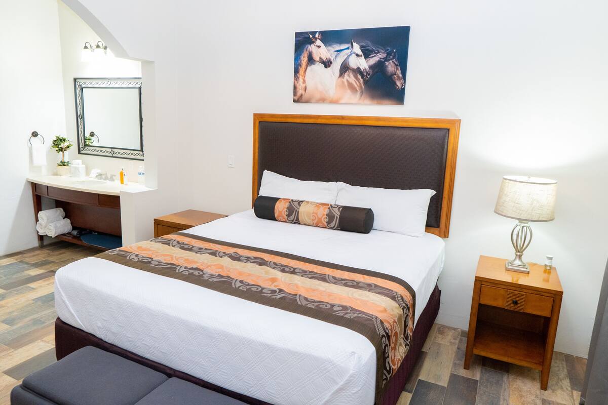 Quarto de hotel bem organizado, com cama, mesa de cabeceira, abajur e espelho.