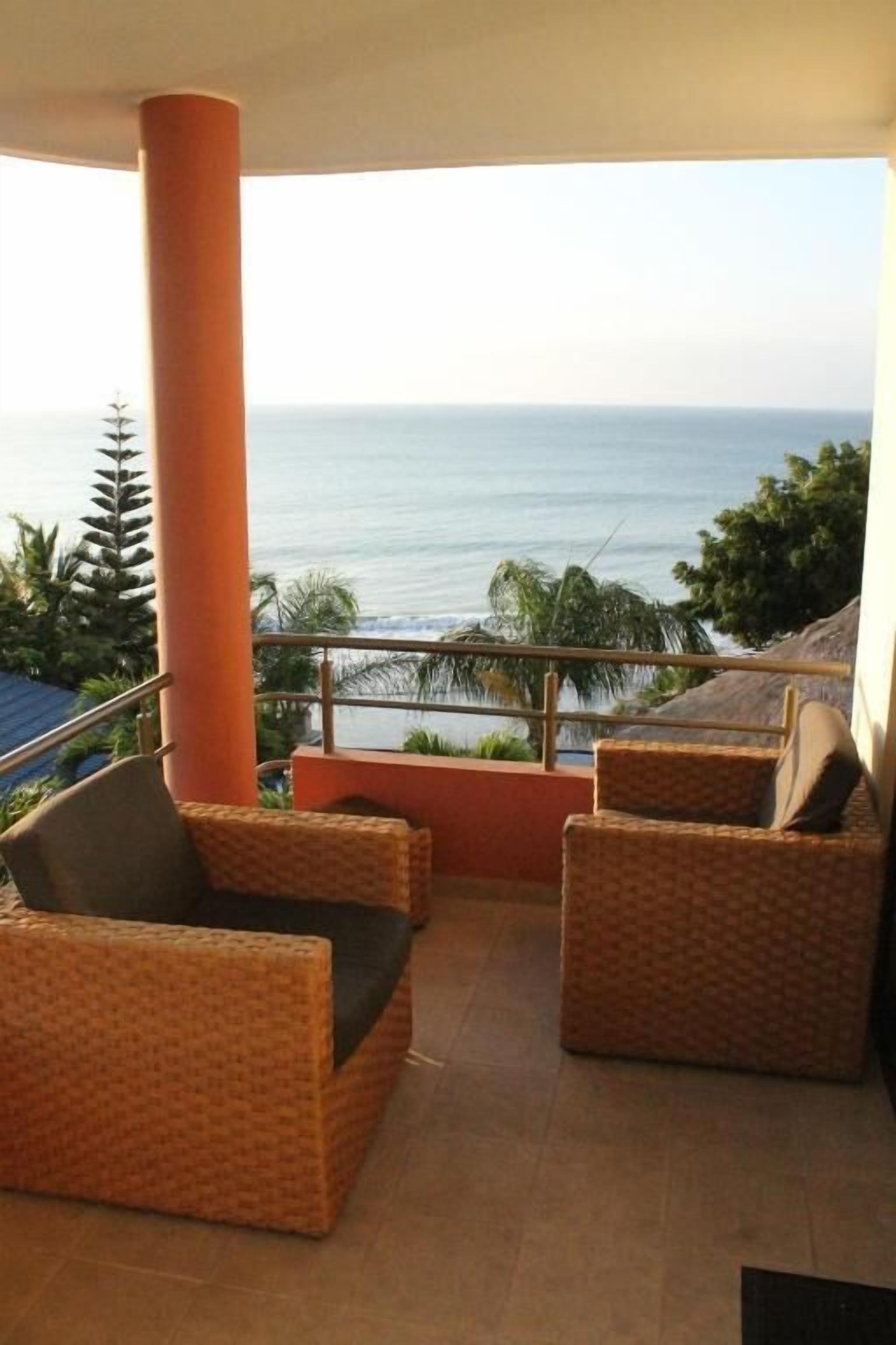 Varanda com móveis de vime e vista para o mar.