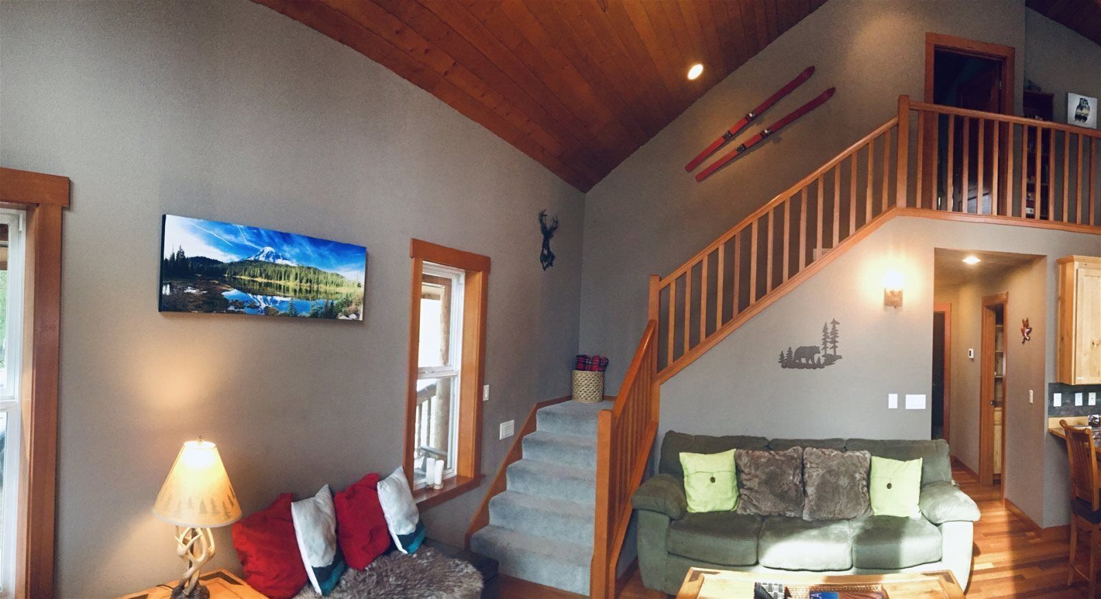 Ampla sala de estar com escada, sofá verde e pintura de uma paisagem montanhosa.