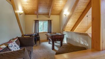 Quarto tipo loft acolhedor, com teto de madeira, mesa de futebol, pequena mesa de jantar e sofá.