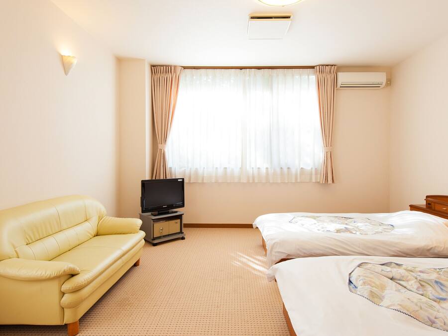 Quarto de hotel com sofá, televisão sobre suporte, cama com colcha florida e janela com cortinas.