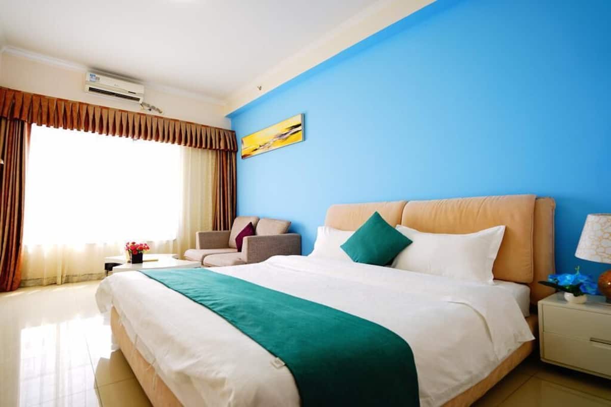 Quarto de hotel com uma cama grande, uma cadeira, uma mesa de cabeceira e uma janela com cortinas.