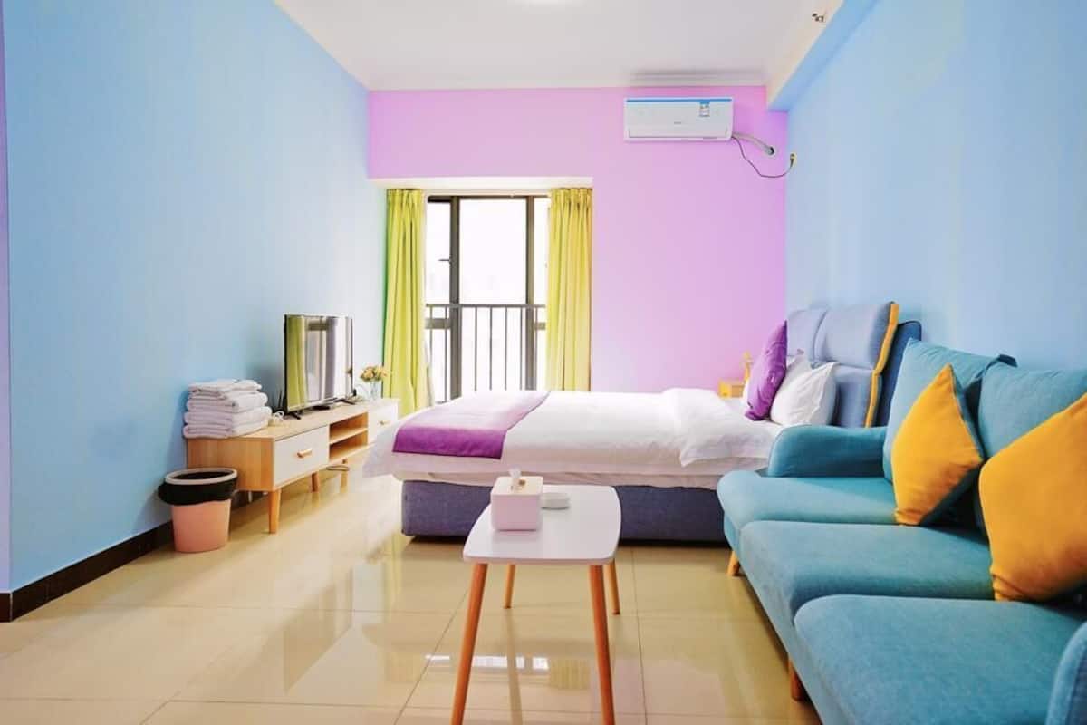 Quarto com cama, sofá, mesinha, televisão e janela com cortinas.