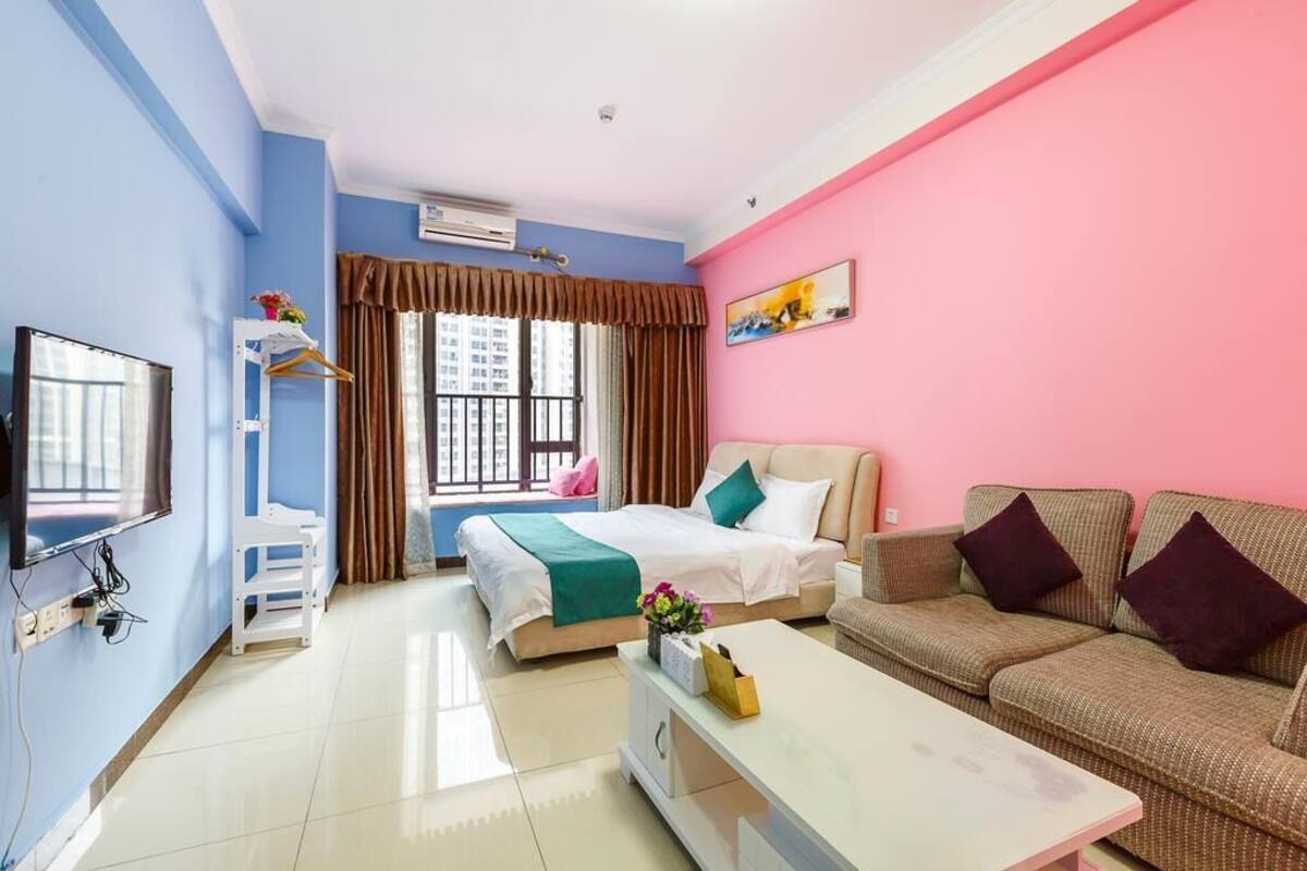 Quarto de hotel com cama, sofá, televisão e janela com cortinas.