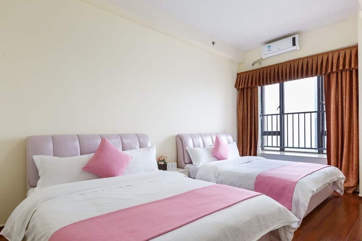 Quarto de hotel com duas camas, cada uma com cabeceira e almofadas, e uma janela grande com cortinas.