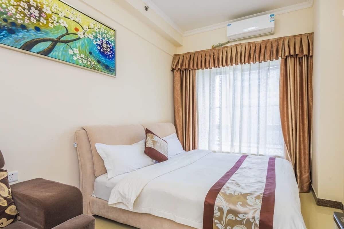 Quarto de hotel com cama, sofá, quadro na parede e janela com cortinas.
